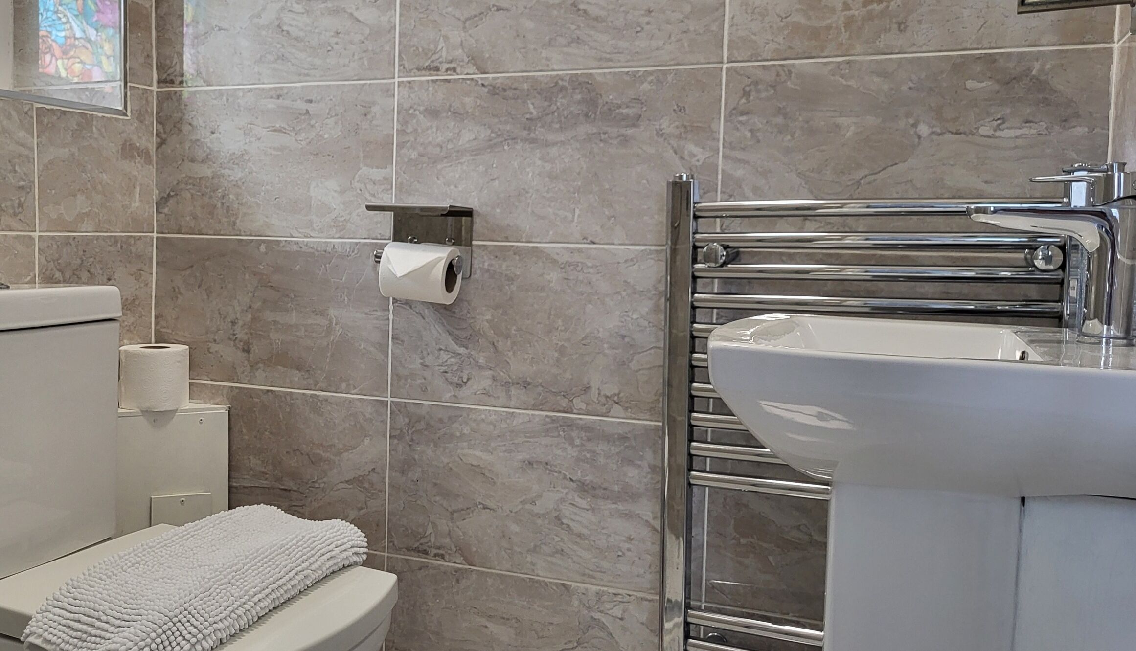 Uma casa de banho moderna com sanita, lavatório e suporte para toalhas.