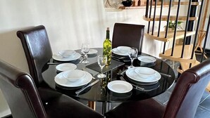 Mesa de jantar com seis cadeiras, uma garrafa de vinho e pratos postos para uma refeição.