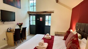 Quarto de hotel com uma cama, uma secretária com uma chaleira, uma cadeira, uma televisão e uma porta com um aviso.