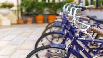 Uma fileira de bicicletas estacionadas em área externa com plantas em vasos e piso de azulejos.