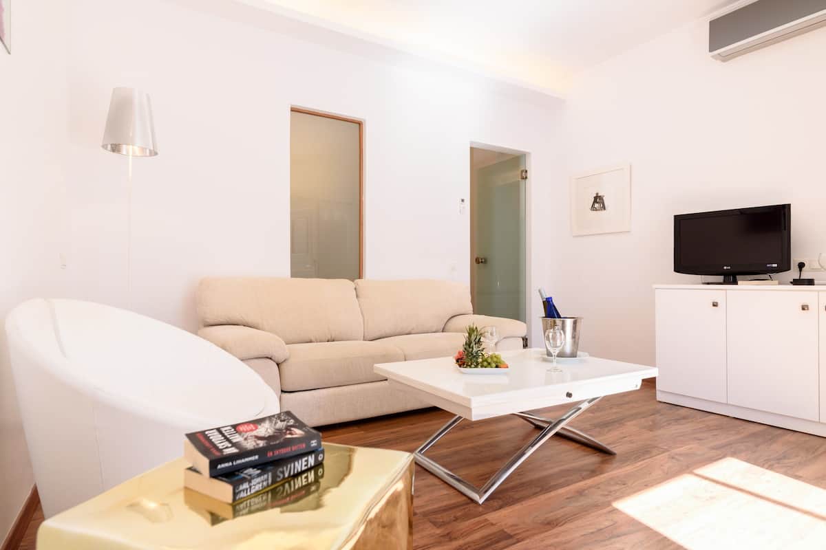 Uma sala de estar moderna com um sofá branco, uma mesa de centro com livros, uma televisão e um armário.