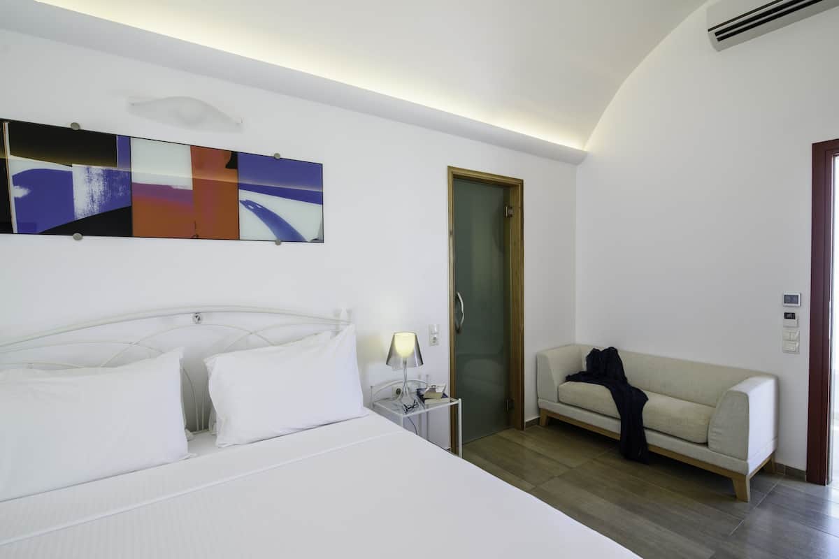 Quarto de hotel com cama, mesa de cabeceira, abajur e sofá.