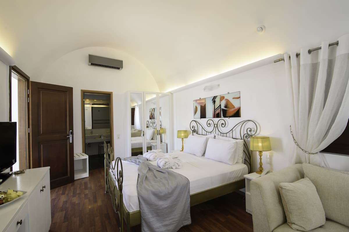 Quarto de hotel com cama, abajures, televisão e sofá.