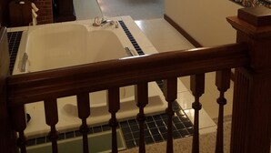 Uma escadaria leva a uma área de refeições com parede de tijolos, um candelabro e piso ladrilhado.