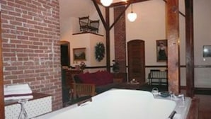 Quarto com uma banheira grande, paredes de tijolo, vigas de madeira e luminárias pendentes.