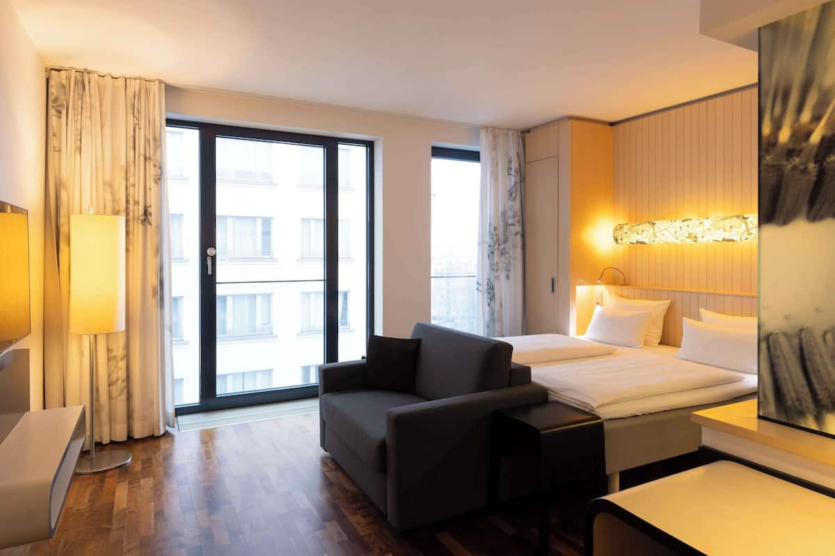 Quarto de hotel com sofá, cama, escrivaninha e uma grande janela.