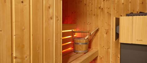Uma sauna de madeira com um banco, um balde e um aquecedor de sauna visíveis.