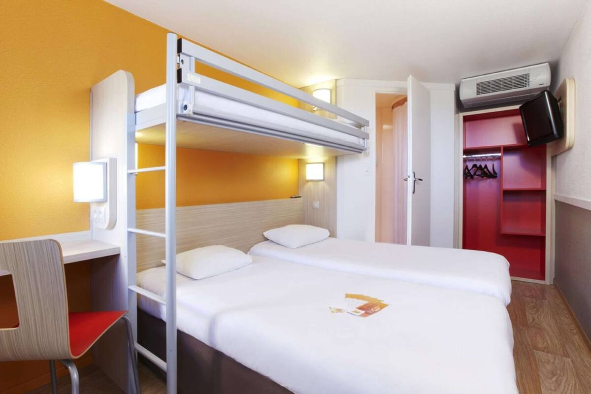 Quarto de hotel com beliche, uma escrivaninha com cadeira, televisão e guarda-roupa.