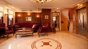 Um hall de entrada luxuoso com um imponente candelabro, confortáveis sofás vermelhos e um piso de mármore.