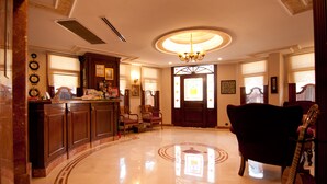 Um hall amplo com piso de mármore, um lustre imponente e um balcão de recepção.