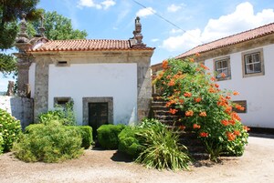 Um edifício tradicional com telhado de telhas, pequena entrada e um jardim com diversas plantas e flores.