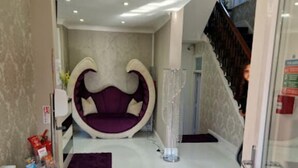 Um hall moderno com uma mesa de recepção, um sofá roxo e uma escadaria para os andares superiores.