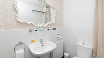 Casa de banho com lavatório branco, espelho com moldura ornamentada, sanita e porta-toalhas.