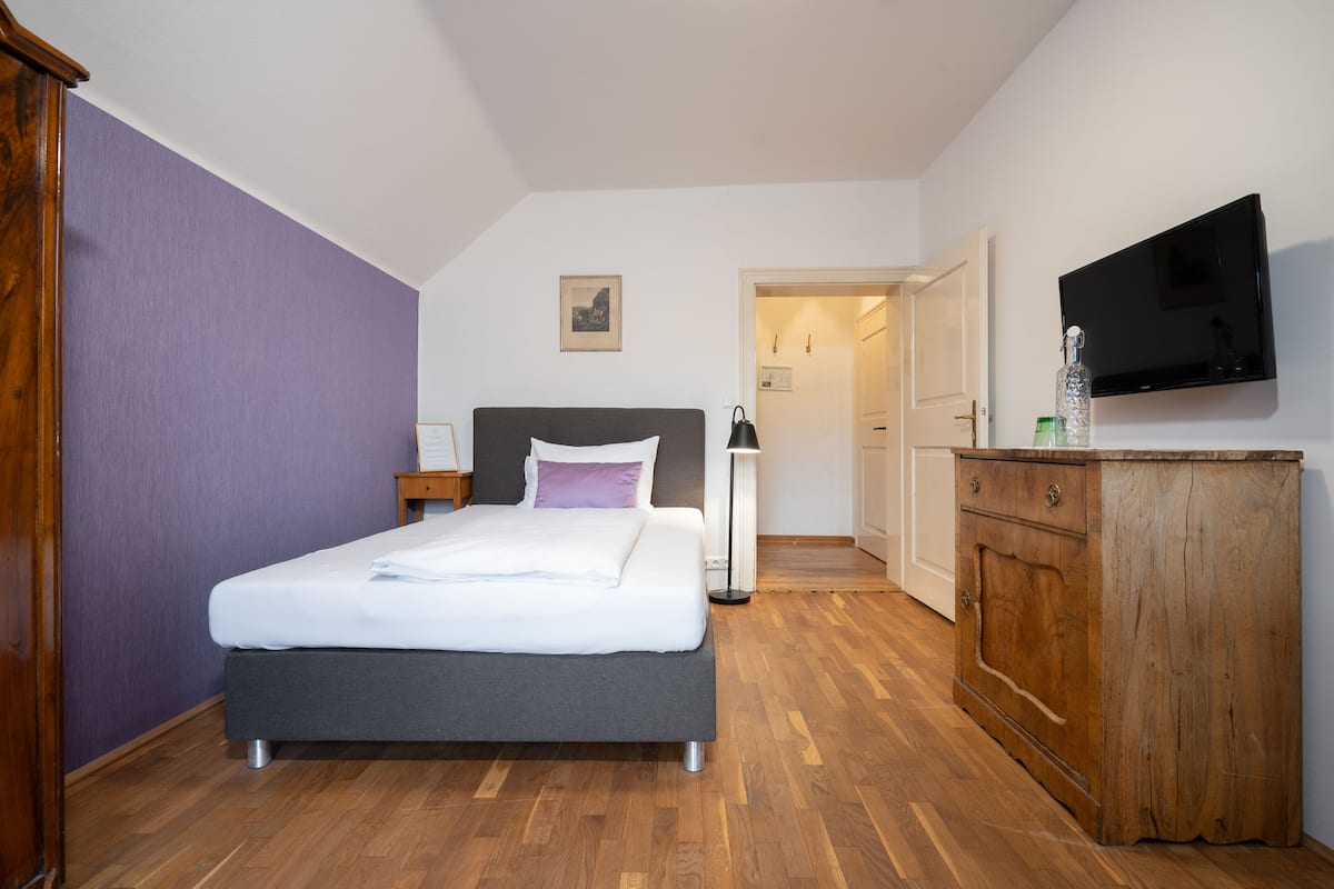 Quarto com cama, cómoda de madeira e televisão na parede.