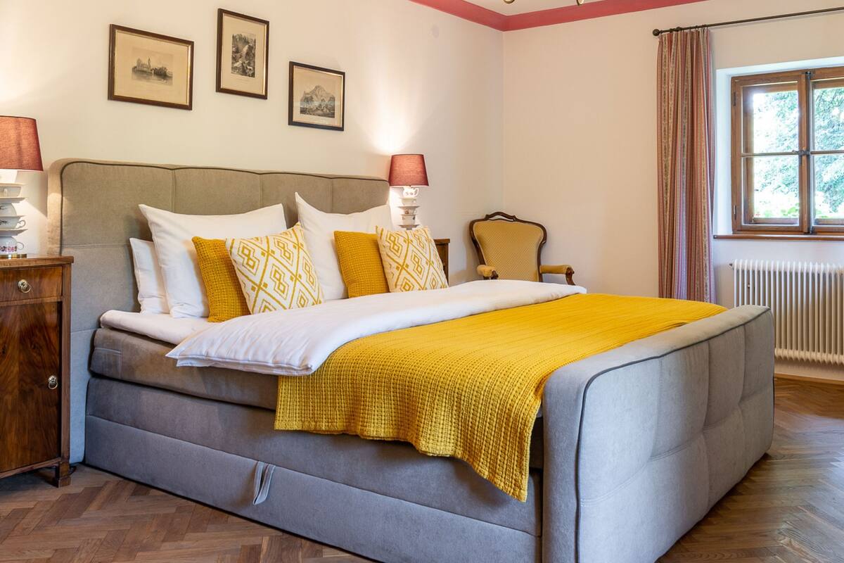 Quarto bem arrumado com cama, mesa de cabeceira, abajur e quadros na parede.