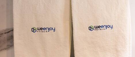 Duas toalhas brancas com o logotipo 'Weenjoy Hotels' penduradas em uma parede de mármore.