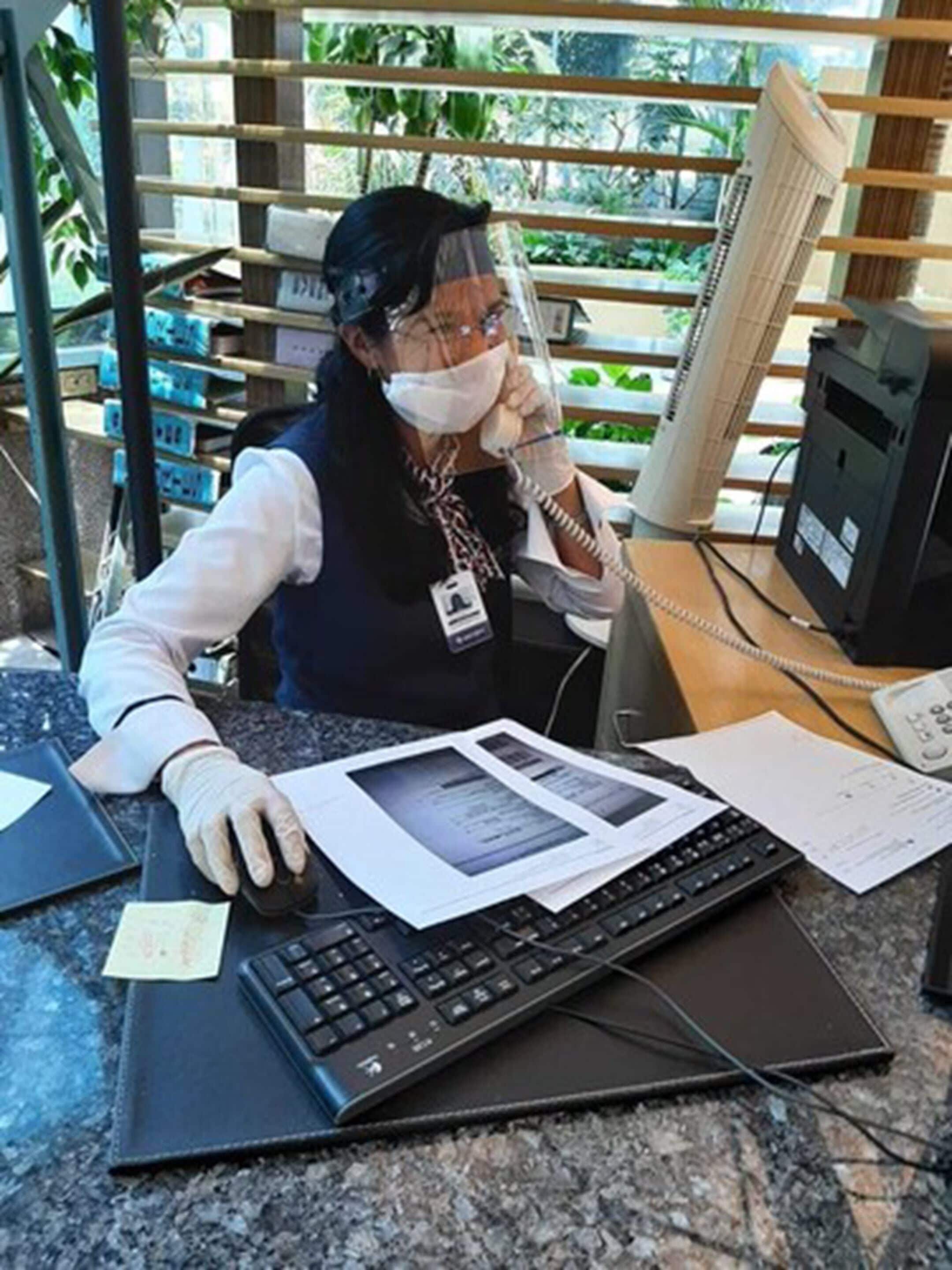 Uma pessoa em uma mesa com um computador, papéis e um telefone.