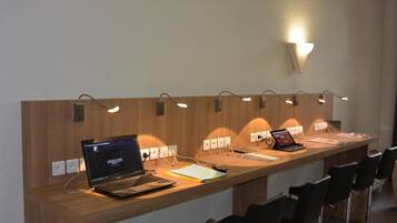 Um balcão de recepção comprido com vários laptops, um bloco de notas e uma caneta, iluminado por luzes fixadas na parede.