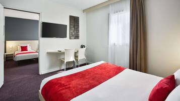 Quarto de hotel com uma cama grande, uma escrivaninha e uma cadeira. Há uma televisão na parede e uma janela com cortinas.