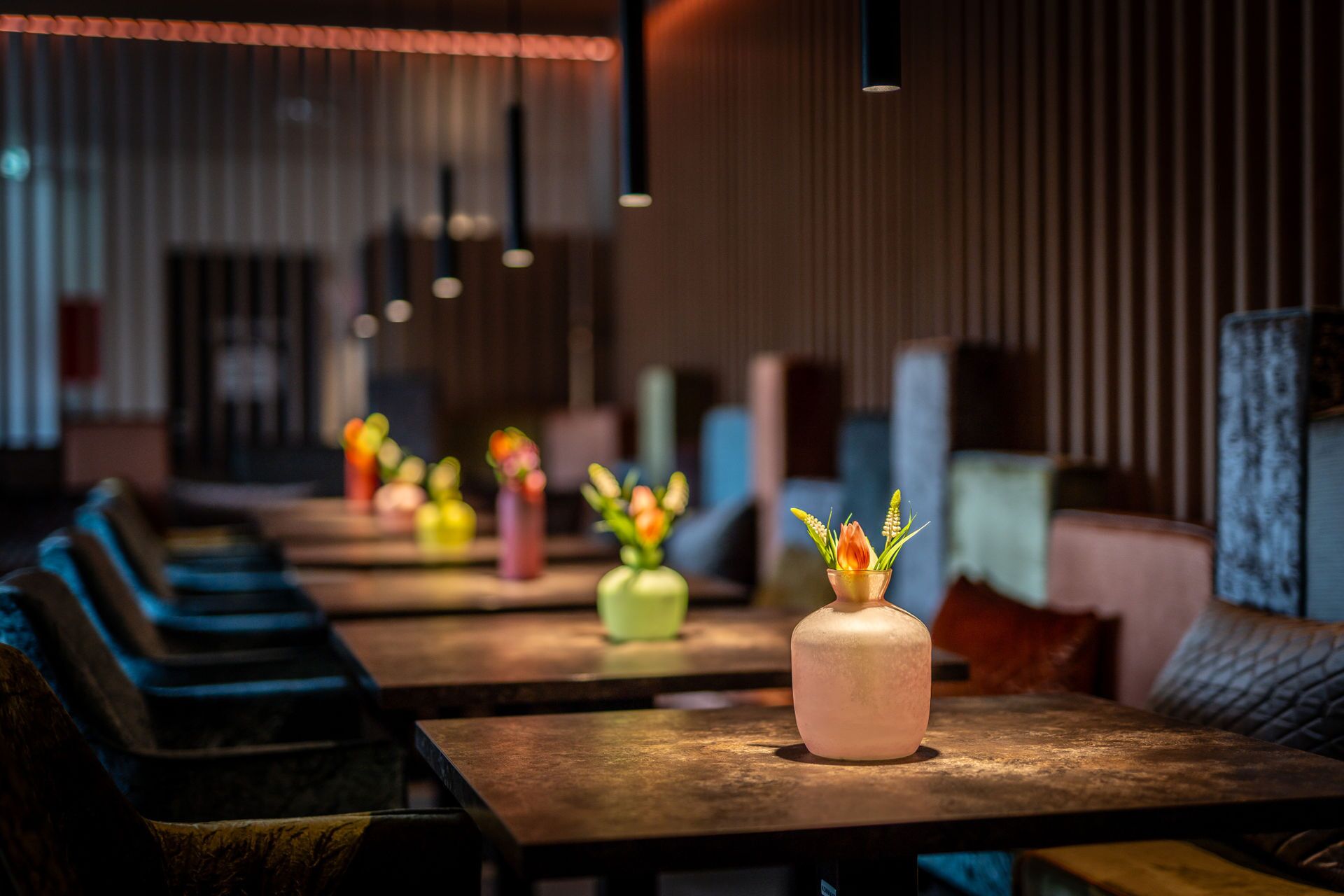 Restaurante com mesas e cadeiras de madeira, cada uma com um pequeno vaso de flores.