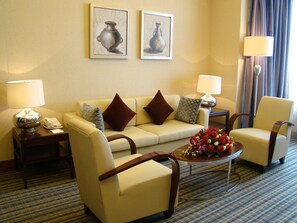 Quarto de hotel com sofá, duas poltronas, mesa de centro com flores, telefone e duas luminárias.