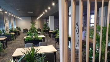 Um espaço de escritório com várias mesas, cadeiras e plantas em vasos.