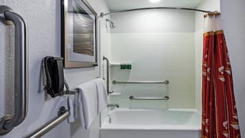 Um banheiro com uma banheira branca, chuveiro com porta de vidro, corrimão, porta-toalhas e telefone.