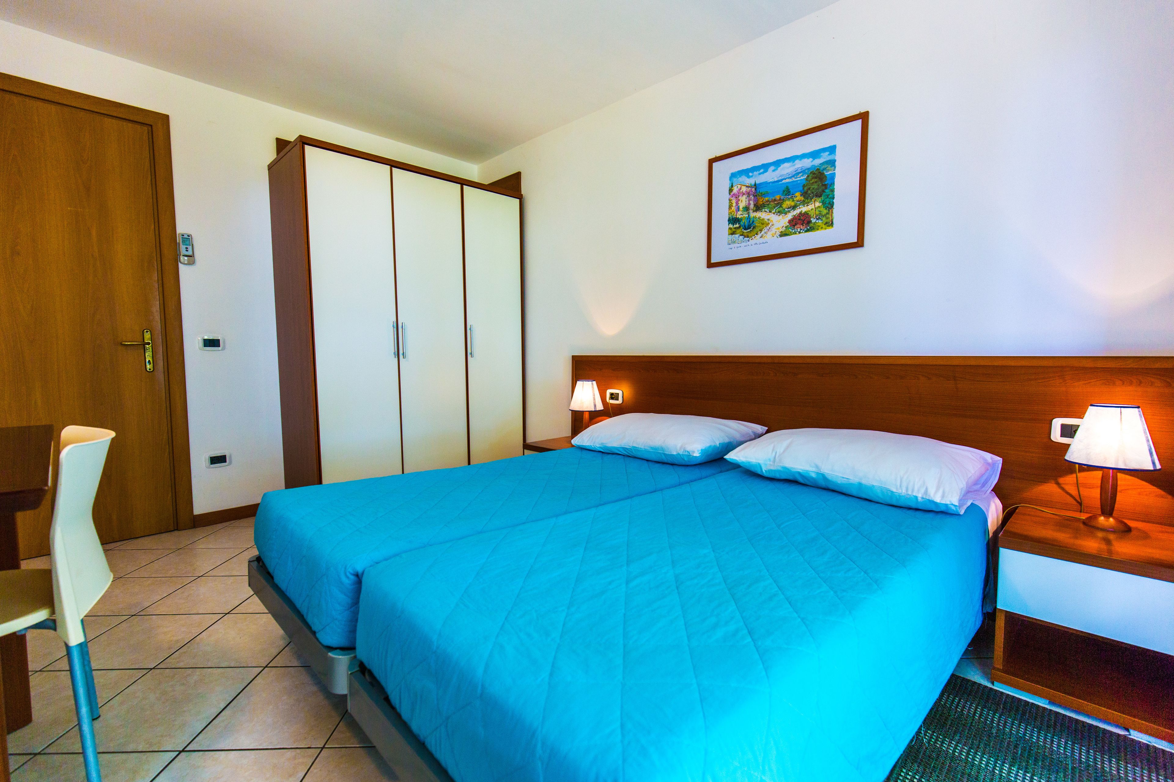 Quarto de hotel com cama, escrivaninha, cadeira, guarda-roupa e um quadro na parede.