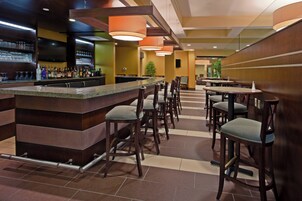 Uma área de bar com balcão, banquetas e um espaço de estar com mesas e cadeiras.
