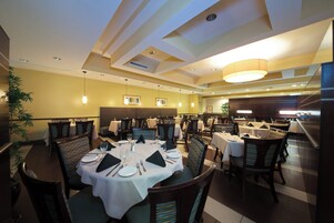 Uma sala de jantar com mesas postas para quatro, cadeiras com estofamento listrado e iluminação pendente.
