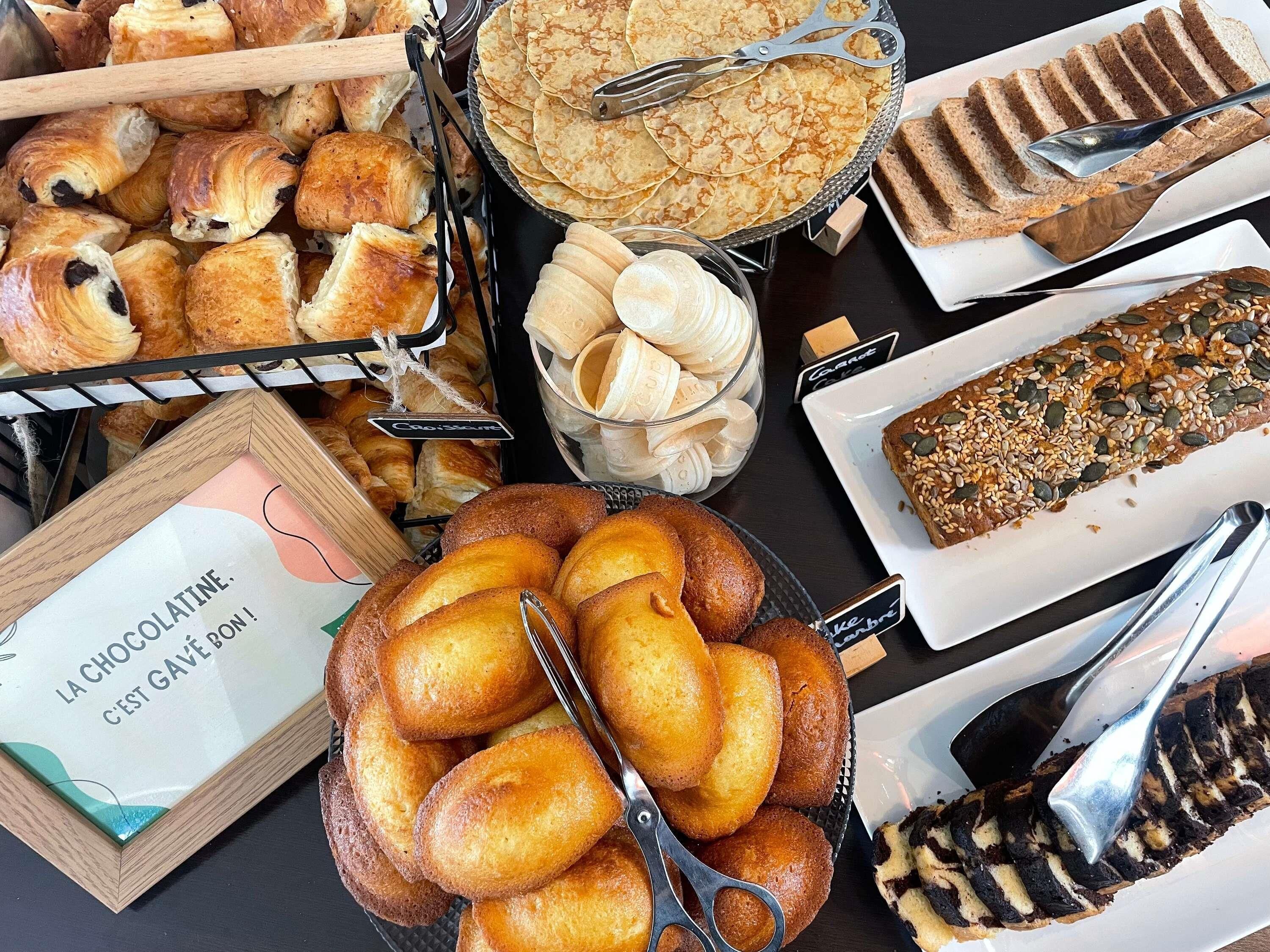 Diversos produtos de panificação, incluindo croissants, pão e um bolo, expostos sobre uma mesa.