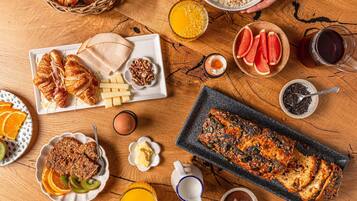 Uma mesa de café da manhã com croissants, queijo, frutas e diversas bebidas.