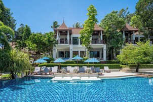 Um hotel com piscina, espreguiçadeiras, guarda-sóis e um jardim tropical.