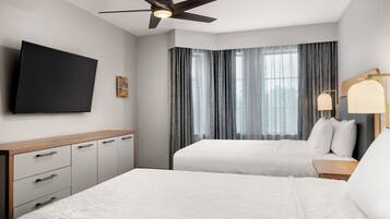 Quarto de hotel com duas camas, televisão de tela plana, ventilador de teto e uma janela grande com cortinas.