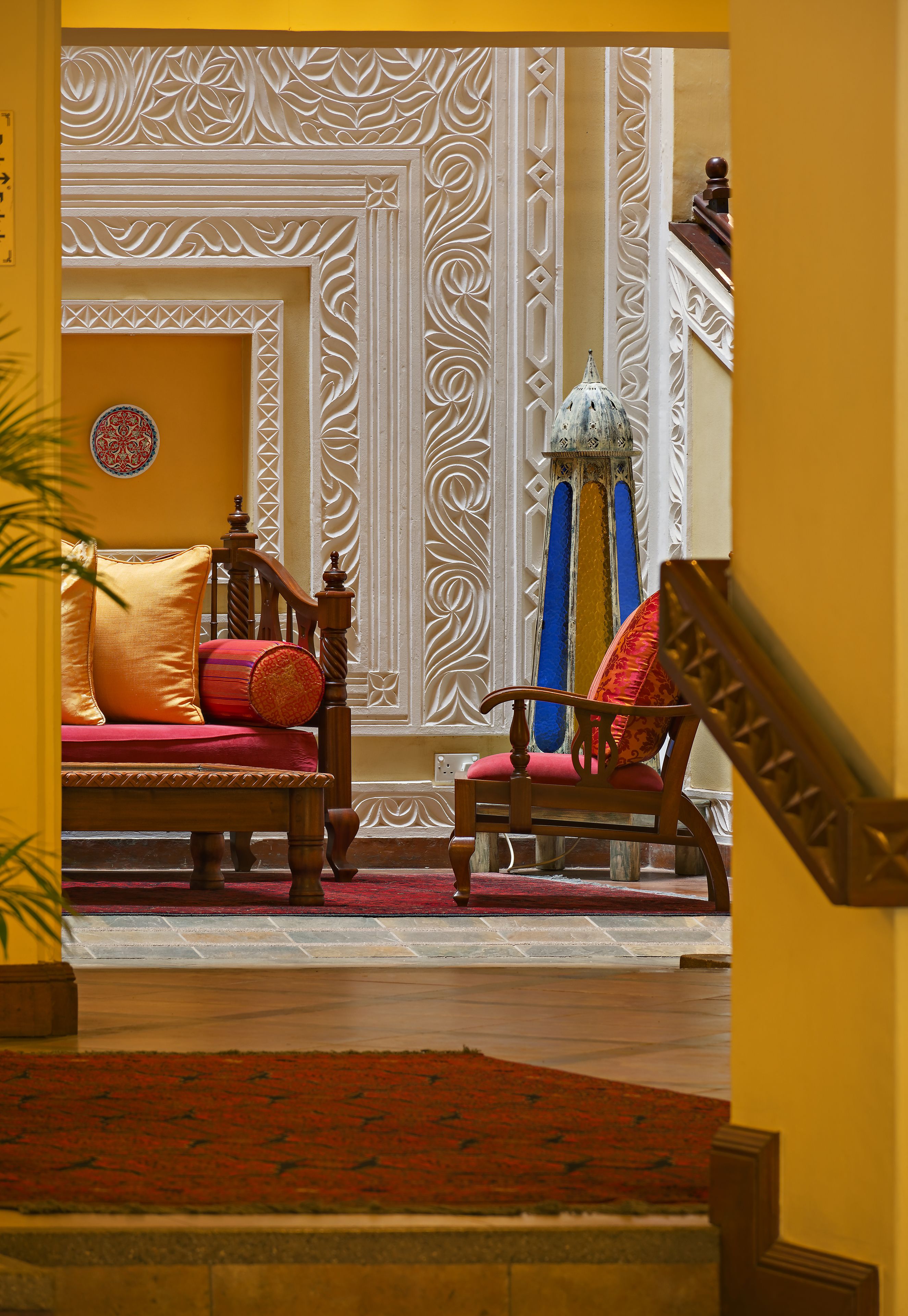 Um interior tradicional com detalhadas esculturas brancas, um sofá vermelho com almofadas, e uma cadeira de madeira com uma almofada vermelha.