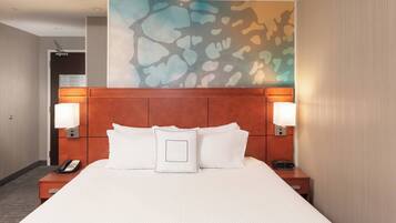 Quarto de hotel com uma cama grande, duas luminárias de cabeceira, um telefone e uma obra de arte na parede.