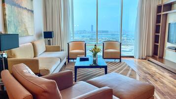 Uma sala de estar moderna com sofá, duas poltronas, uma mesa de centro e televisão. Grandes janelas oferecem vista para a cidade.