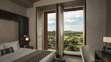Quarto de hotel com uma cama grande, uma mesa com telefone e vista para um campo de golfe.