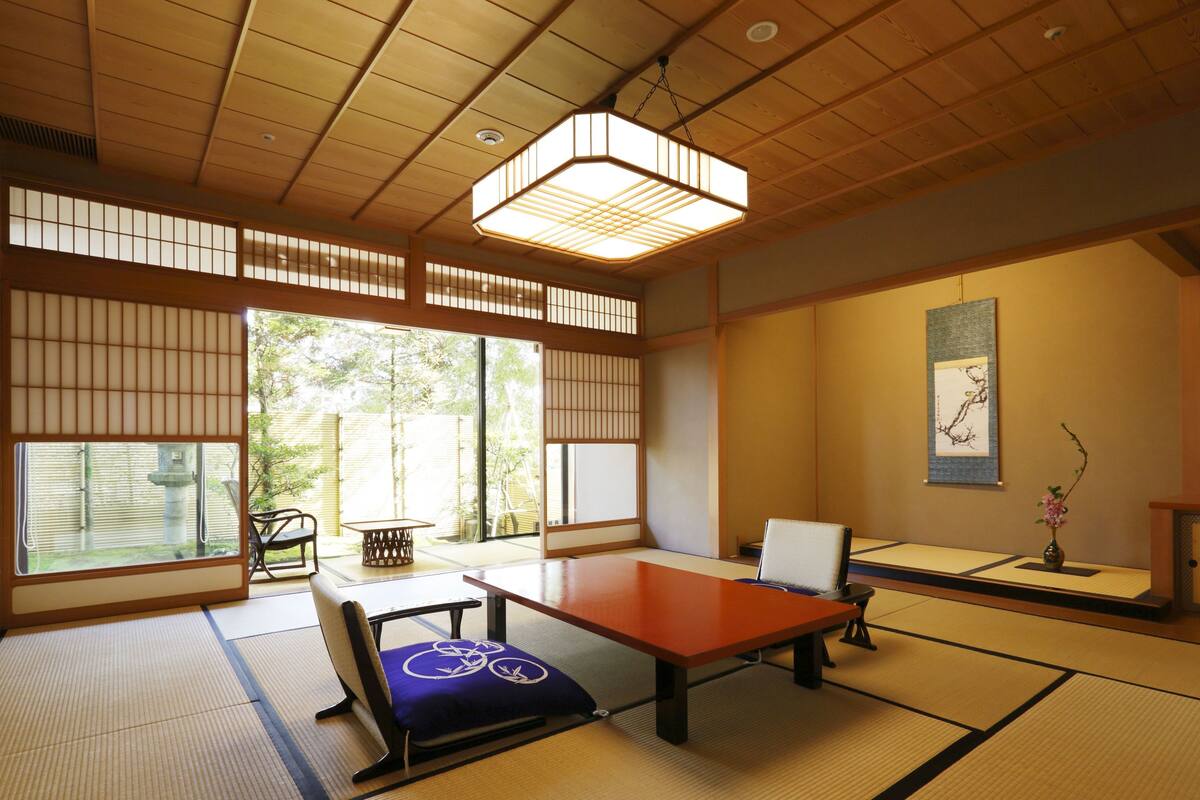 Quarto japonês tradicional com tatames, uma mesa baixa e uma cadeira com almofada.