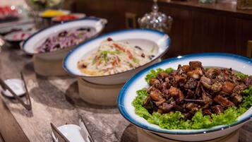 Uma mesa de buffet com diversos pratos, incluindo uma saladeira com carne desfiada sobre alface, uma salada de legumes e outros alimentos.