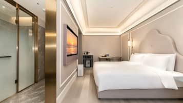 Quarto de hotel com uma cama, escrivaninha, cadeira, TV fixada na parede e armário com porta de vidro.