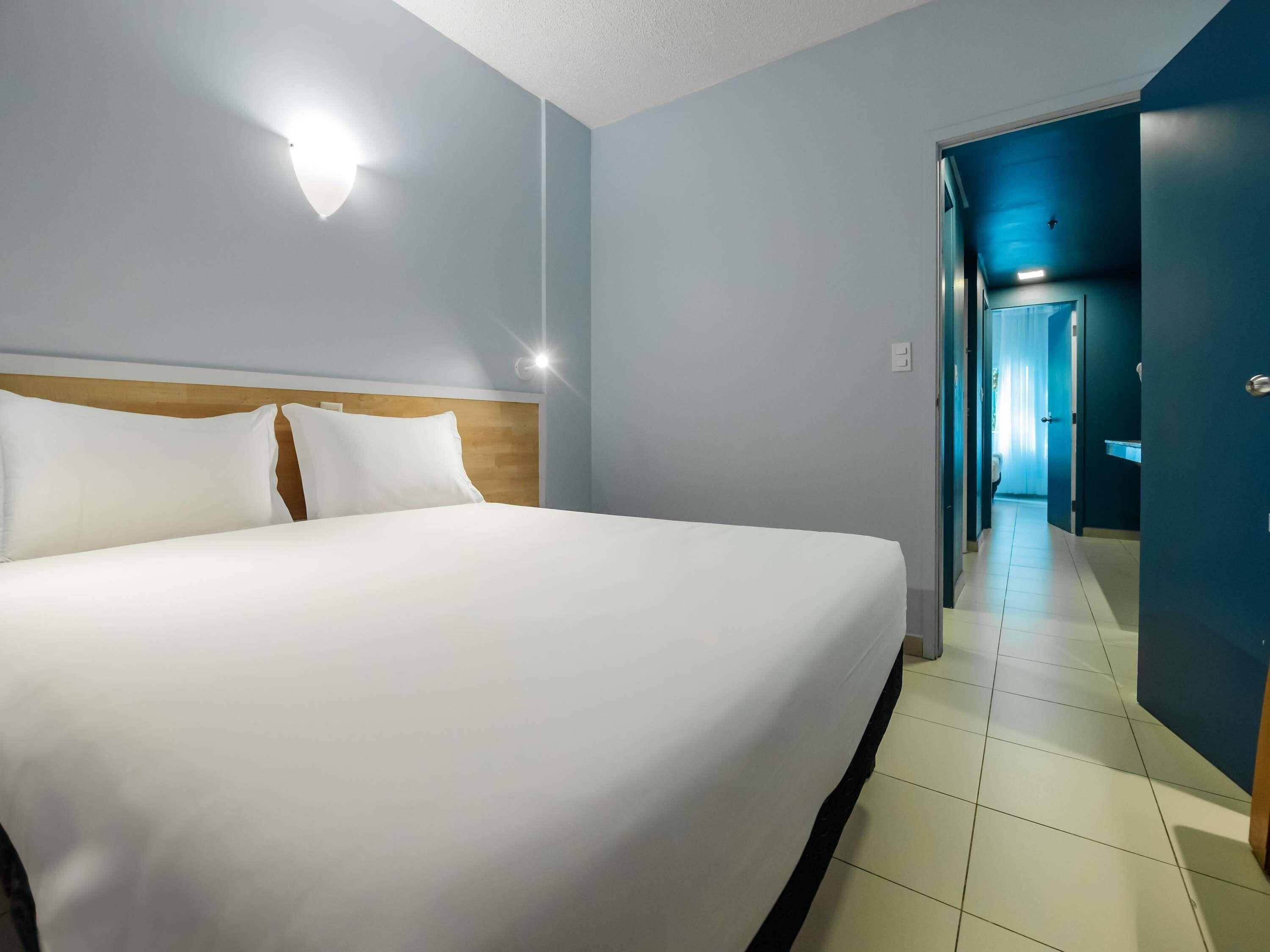 Quarto de hotel com uma cama grande, cabeceira de madeira e piso claro.
