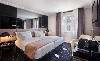 Quarto de hotel com uma cama grande, mesas de cabeceira, escrivaninha com cadeira, máquina de café e janela com cortinas.