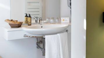 Casa de banho moderna com lavatório branco, espelho e porta-toalhas. Há produtos de higiene pessoal no lavatório e uma cesta de toalhas.