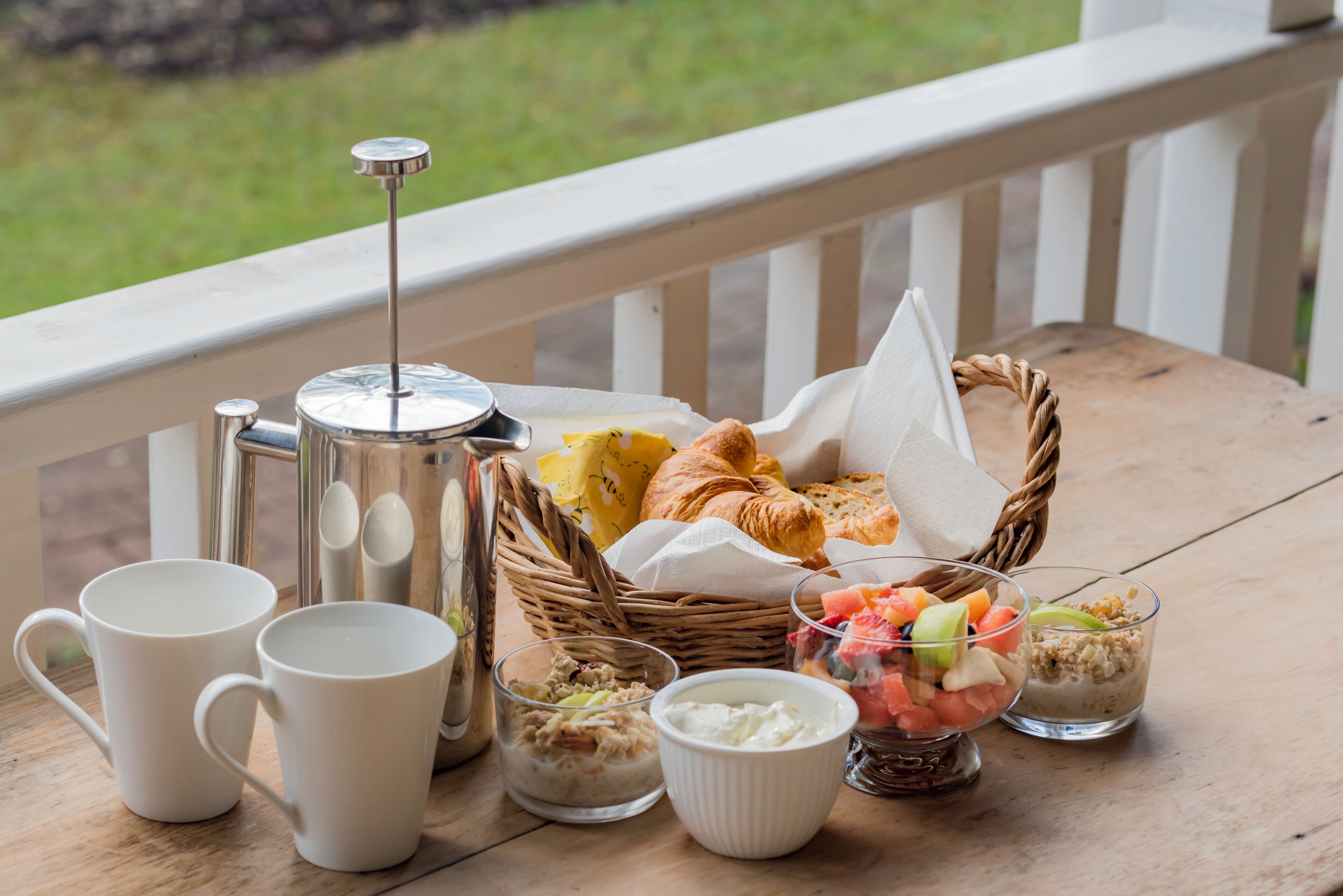 Uma mesa de madeira com uma máquina de café, croissants, frutas e diversos itens de pequeno-almoço.