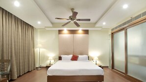 Quarto de hotel com uma cama grande, um ventilador de teto e vista da cidade através de uma janela ampla.