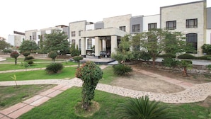 Um edifício moderno com entrada coberta, caminhos pavimentados e jardins ajardinados.