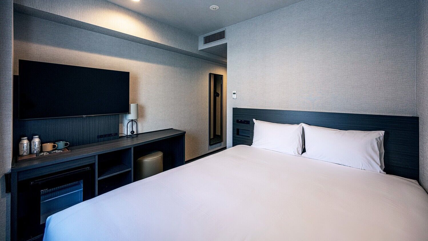 Quarto de hotel com cama, televisão, escrivaninha e espelho.
