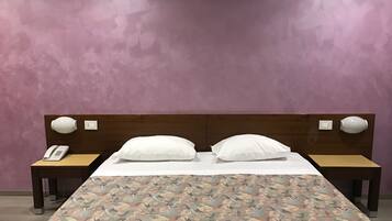 Quarto de hotel com uma cama, duas mesas de cabeceira, um telefone e um abajur fixado na parede.