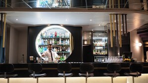 Uma área de bar com um balcão circular de garrafas, banquetas e um bartender.